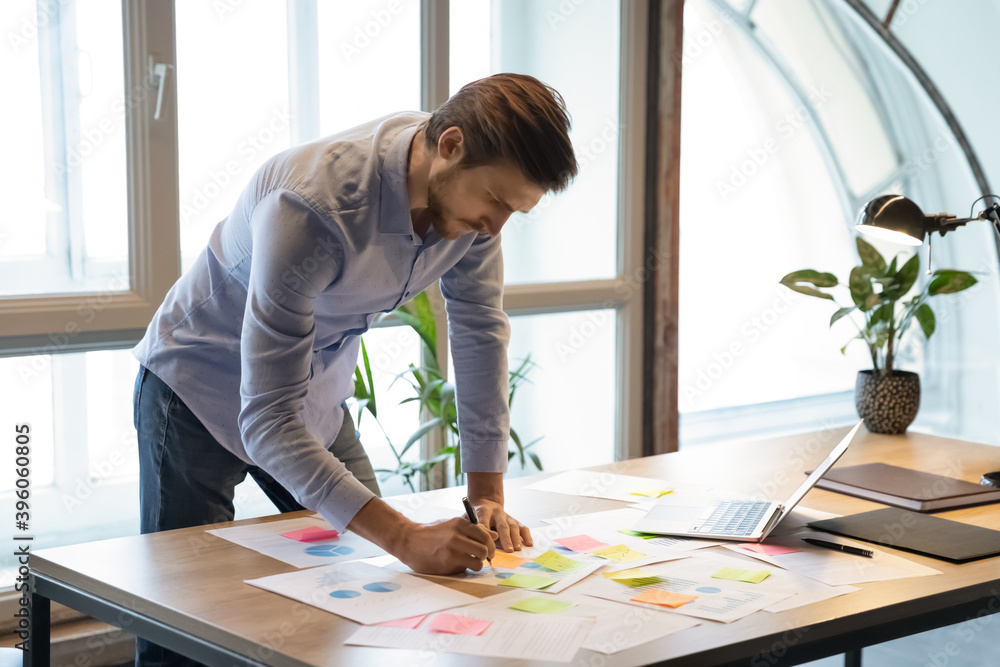 Thoughtful serious young businessman employee standing at desk focused ...