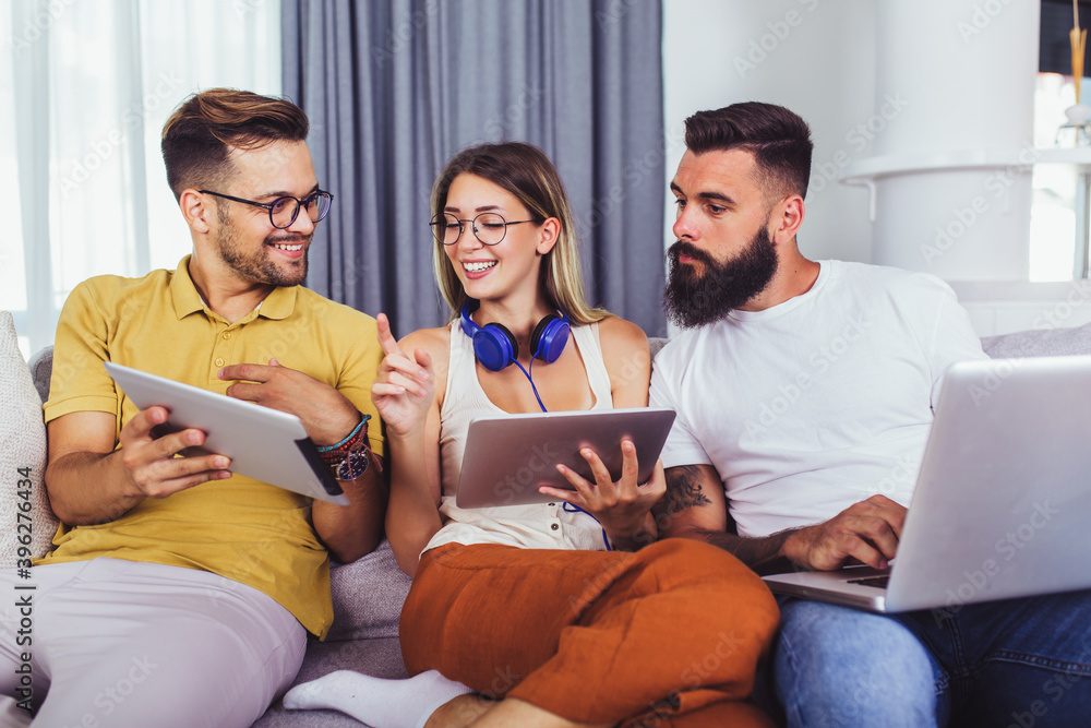 Friends using their digital device sitting on a couch in the living ...