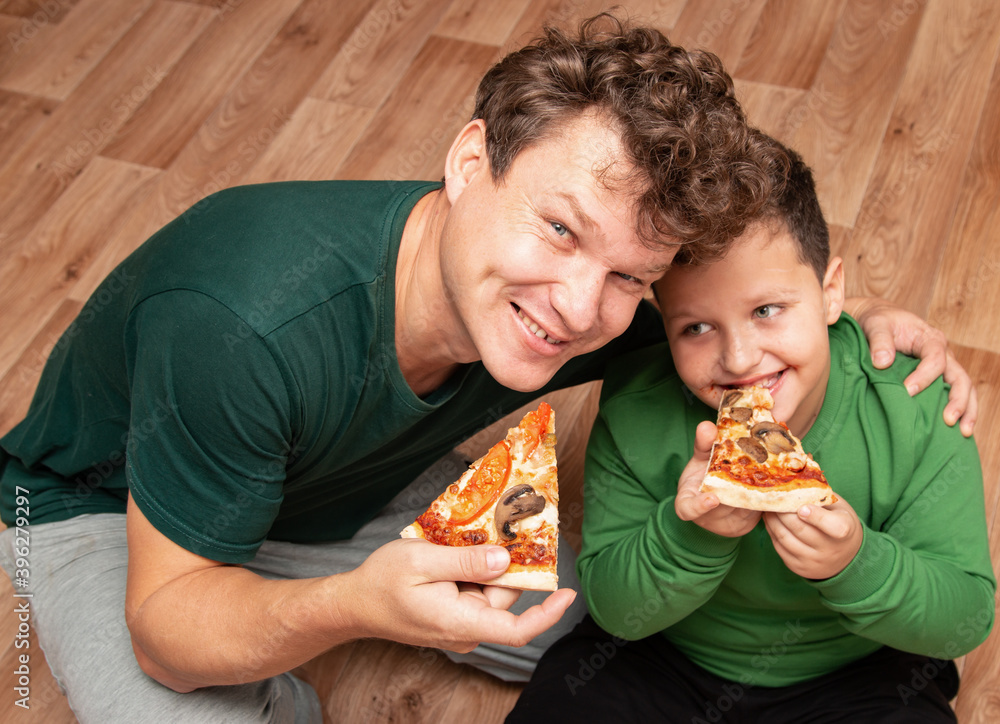 Foto de son and dad eat pizza at home do Stock | Adobe Stock