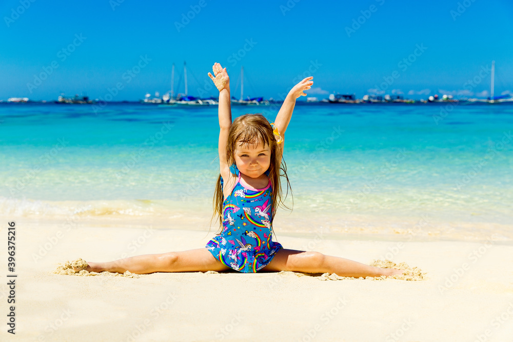 Smiling little girl doing gymnastics splits on a sandy tropical beach ...