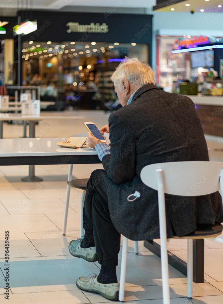 Back view of an old man 70-75 years sitting in a cafe and using his ...