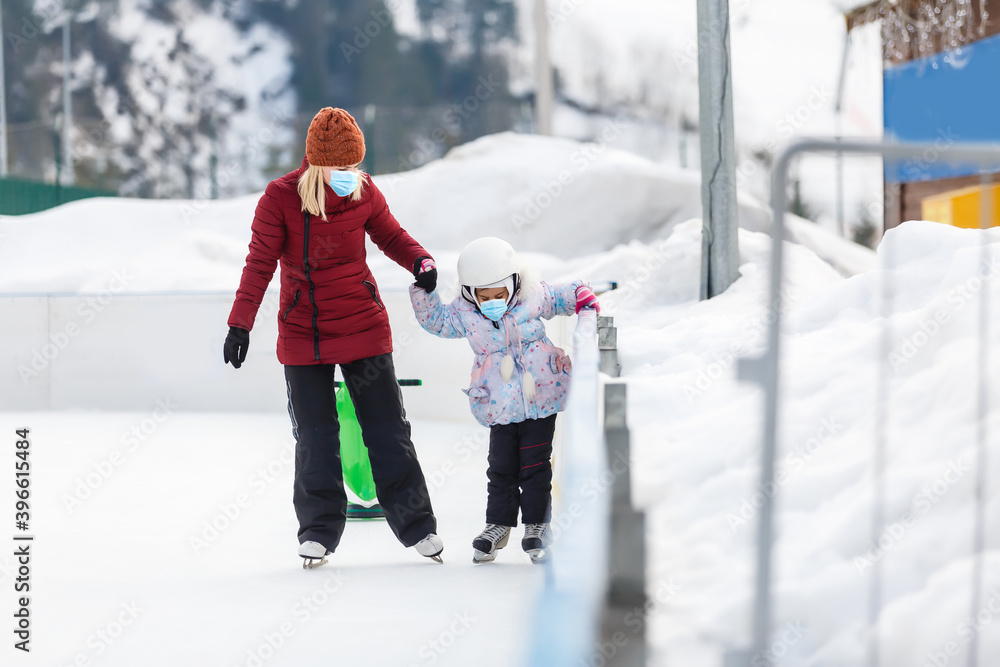young mother teaching her little daughter ice skating at outdoor ...