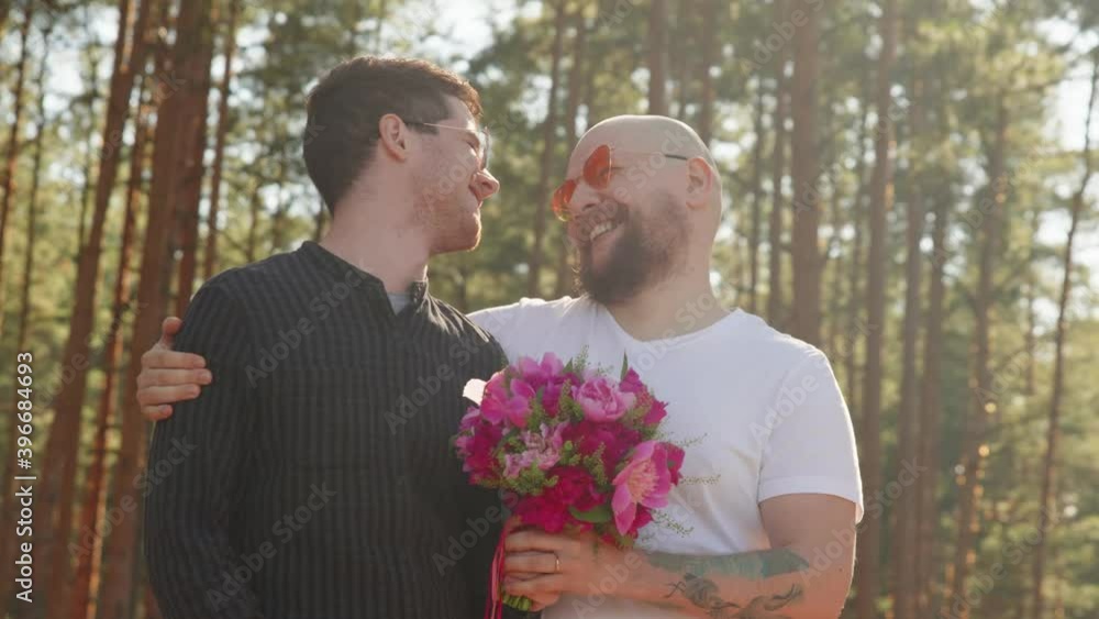 Two men with flower bouquet and ring on finger smile and hug. Gay ...