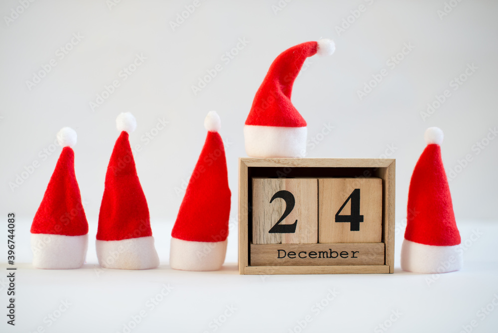 Cube wooden calendar showing date on 24th December with small Santa hats over white background ...