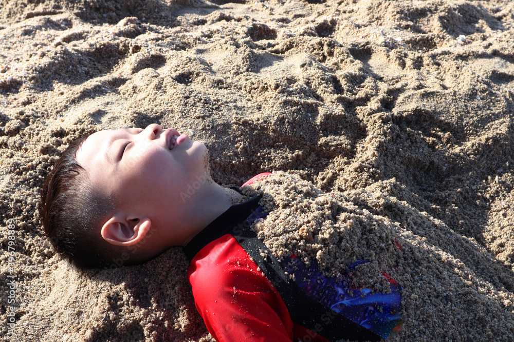 an asian short hair young kid boy is enjoy playing sand to bury himself ...