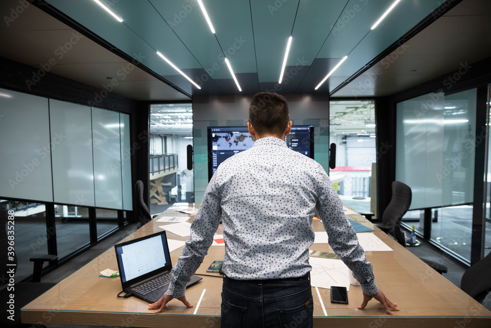 Rearview of man standing facing digital wall screen in meeting room ...