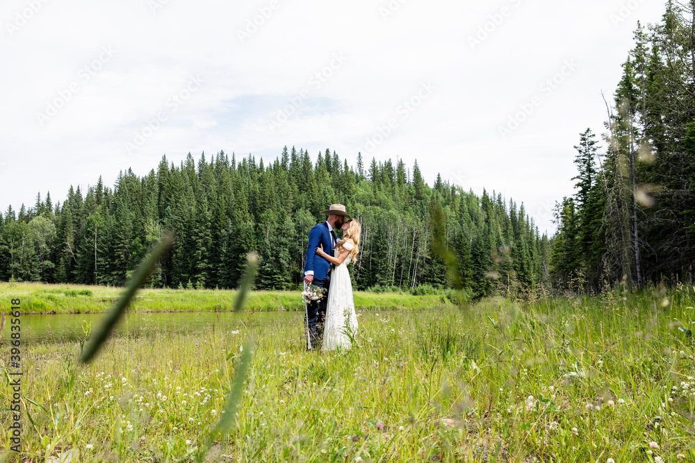 Affectionate bride and groom in cowboy hat kissing at sunny riverside ...