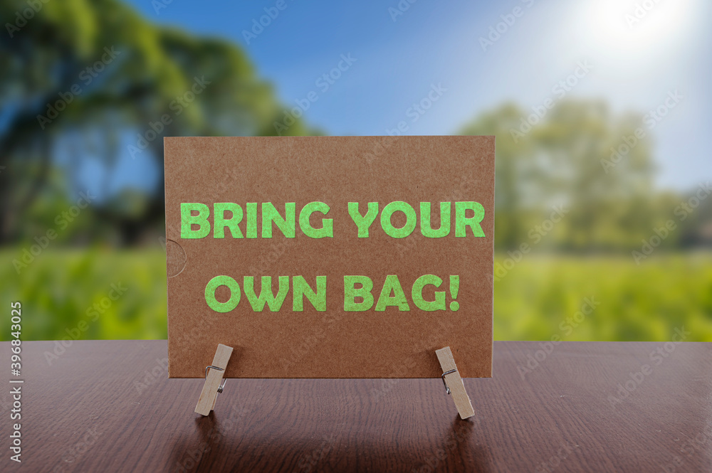 Bring your own bag text on card on the table with sunny green park ...