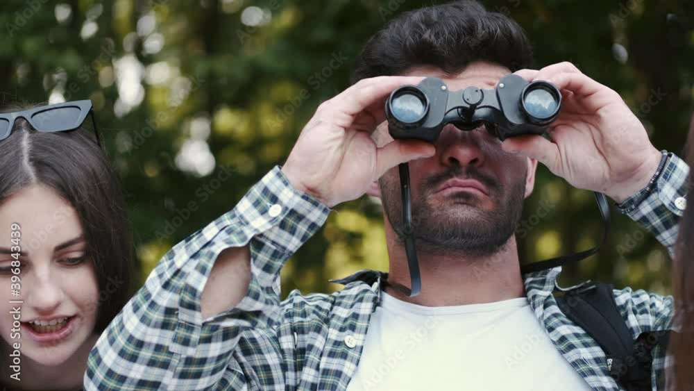 Handsome young man is watching in binoculars while his female friends ...