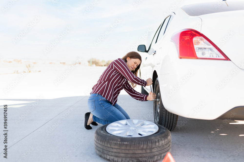 Young woman struggling to change a flat tire on the side of the highway ...