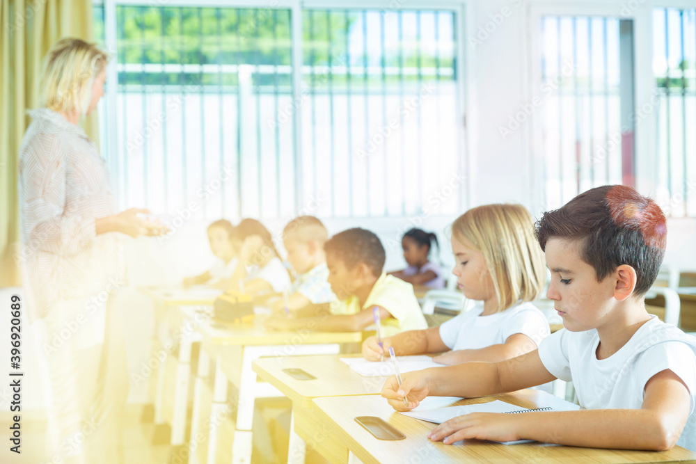 Multiracial group of kids working at class, writing and listening ...