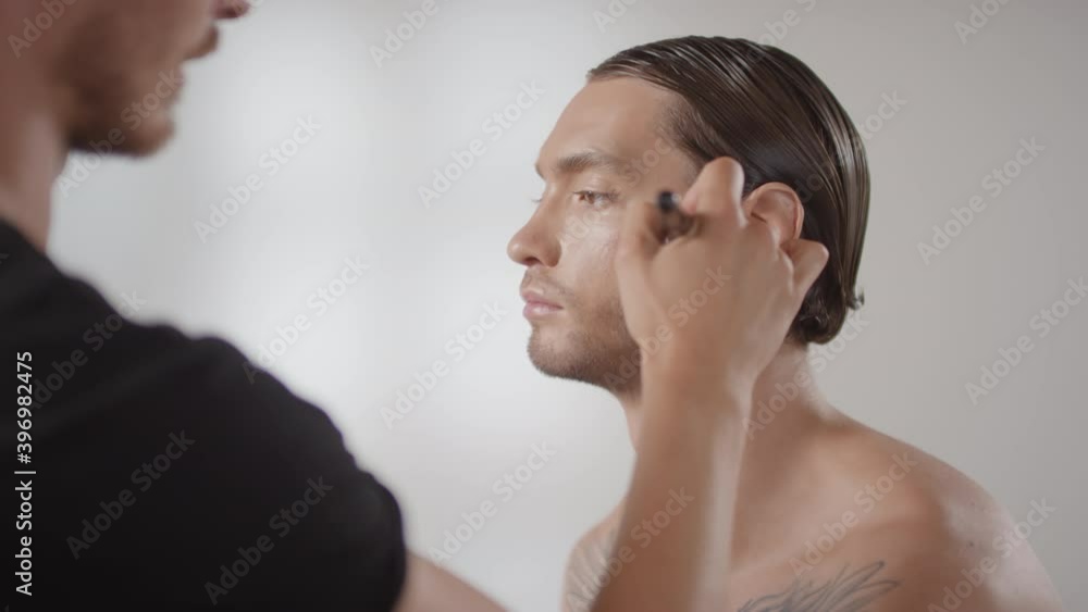 Medium shot of male make-up artist using brush and applying bronzer or ...
