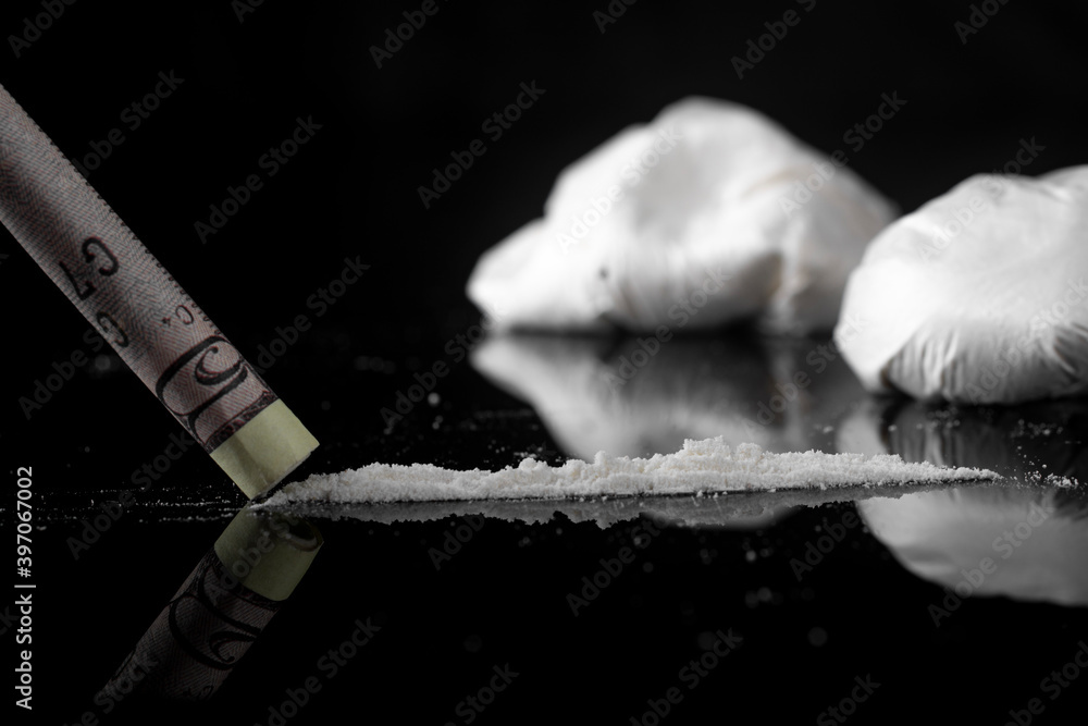 A strip of cocaine and a rolled up banknote on a black background ...