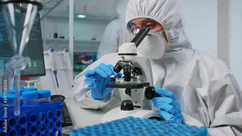 Woman research scientist wearing ppe suit looking at samples under ...