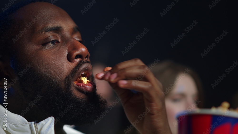 African man eating popcorn in movie theater. Afro guy looking film in ...