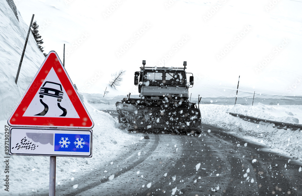 Snowy curvy road with traffic warning signs and winter service vehicle ...