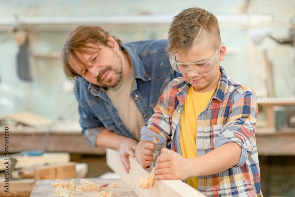 Carpenter teaches young boy to plan wood in a carpentry workshop Stock ...