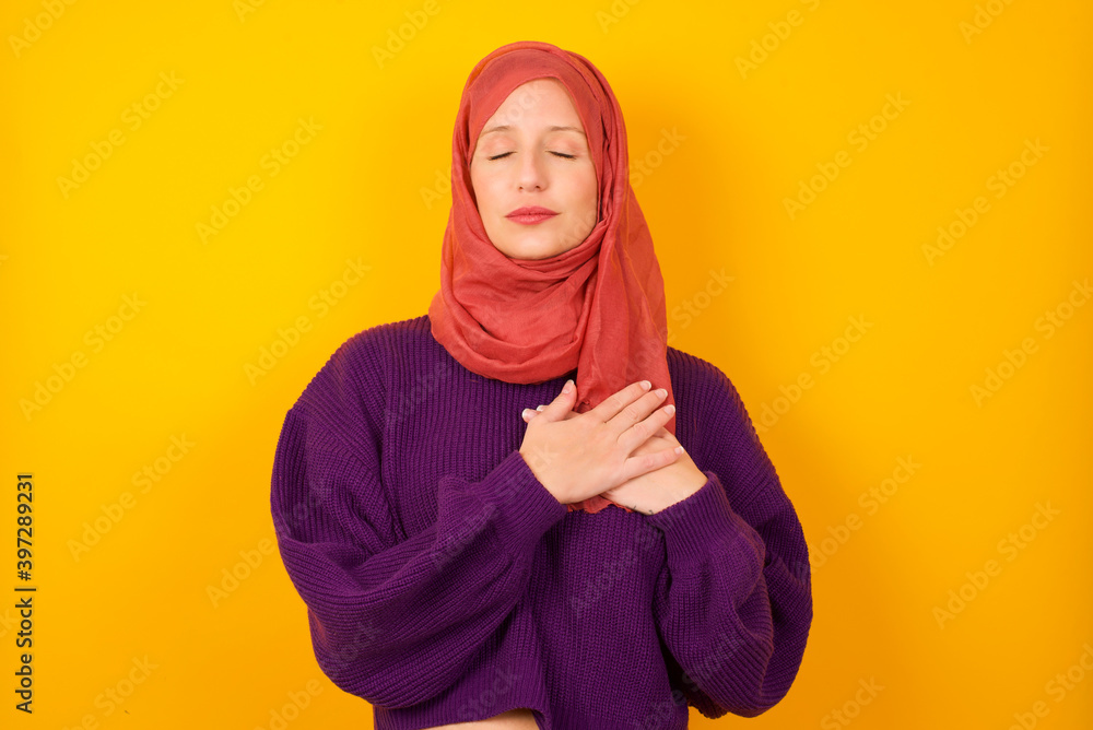 Young caucasian Muslim woman wearing hijab closes eyes and keeps hands ...