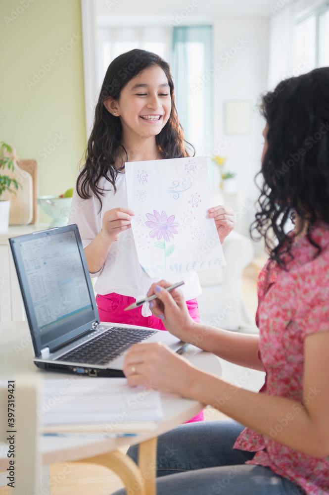 Hispanic girl proudly showing drawing to mother Stock Photo | Adobe Stock