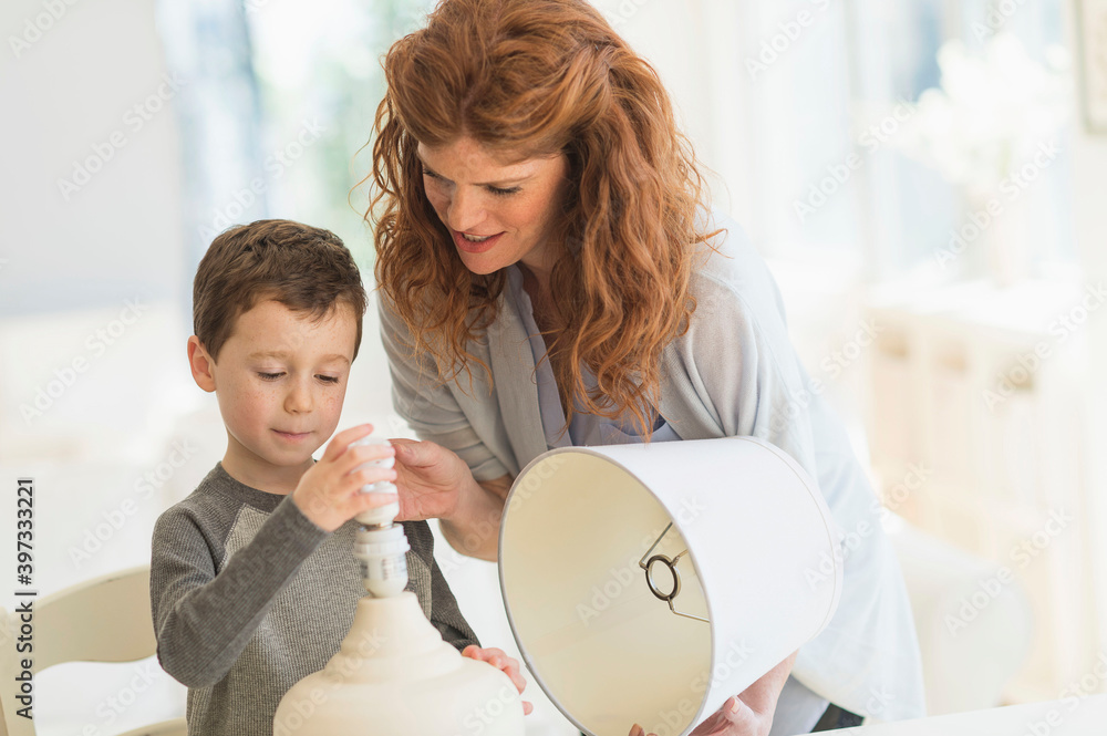 son (6-7) and mother changing lightbulb in table lamp Stock Photo ...