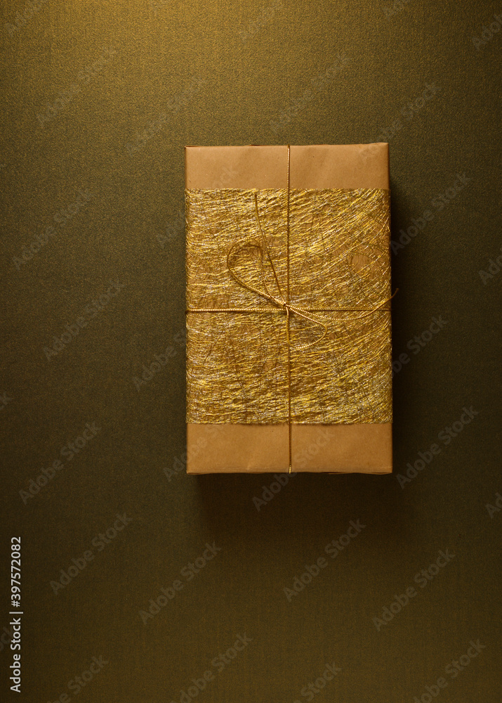 A brown gift box wrapped in a glittering golden wrapping paper, tied ...
