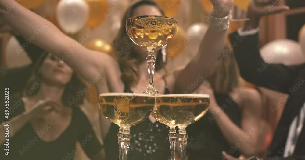 Pyramid of champagne glasses with people dancing around in party ...