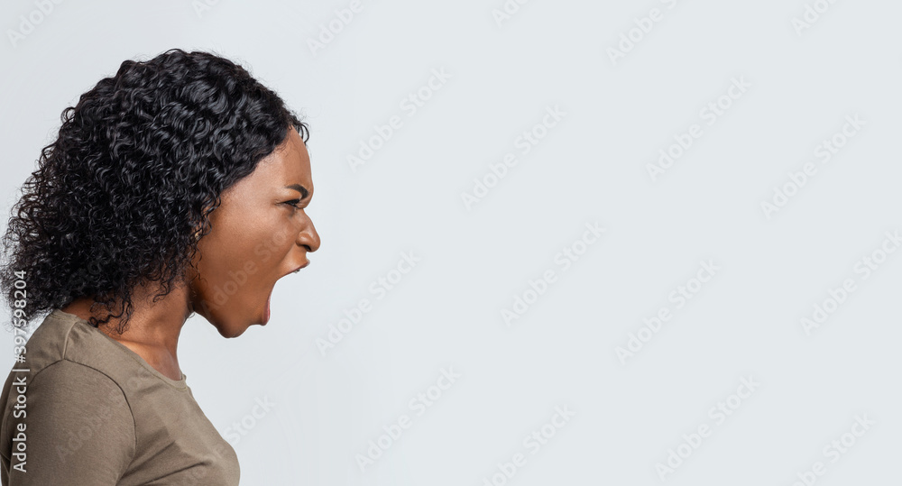 Angry black woman shouting towards copy space over grey background ...