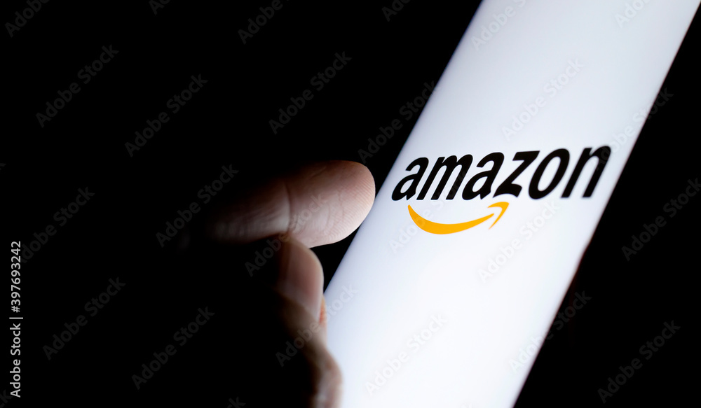 Amazon logo on a smartphone screen in a dark room and a finger pointing ...