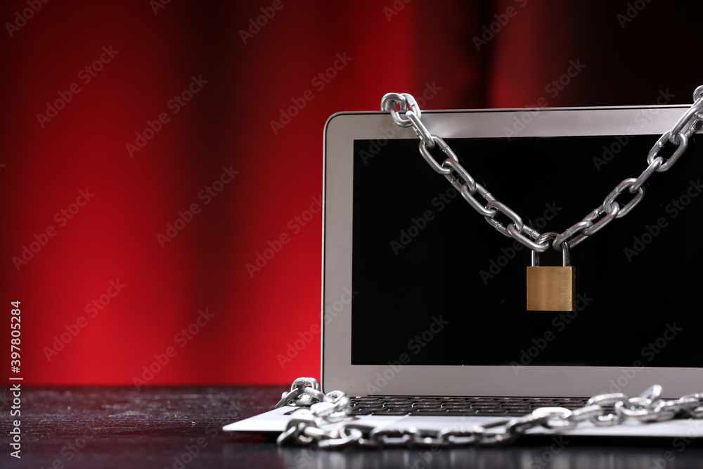 Laptop tied with an iron chain with a lock on a dark office table ...
