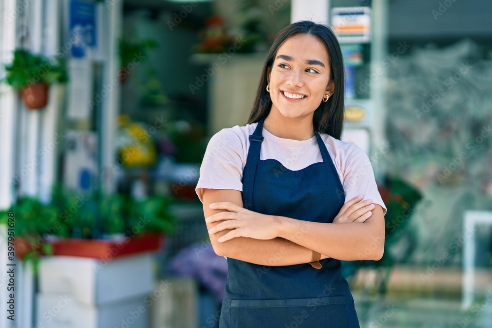 Foto de Young latin shopkeeper girl with arms crossed smiling happy ...