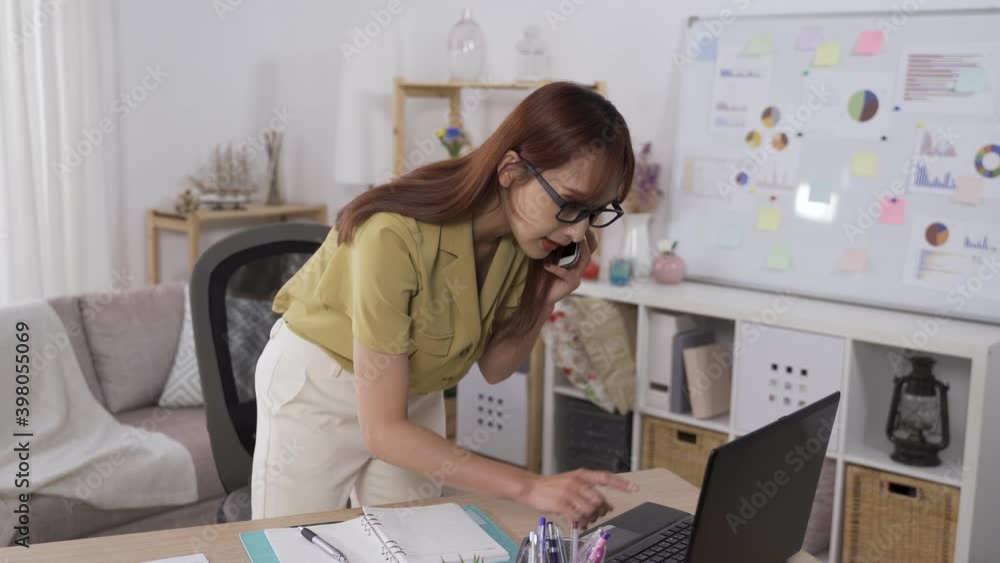 asian assistant standing and bending over laptop with phone call is ...