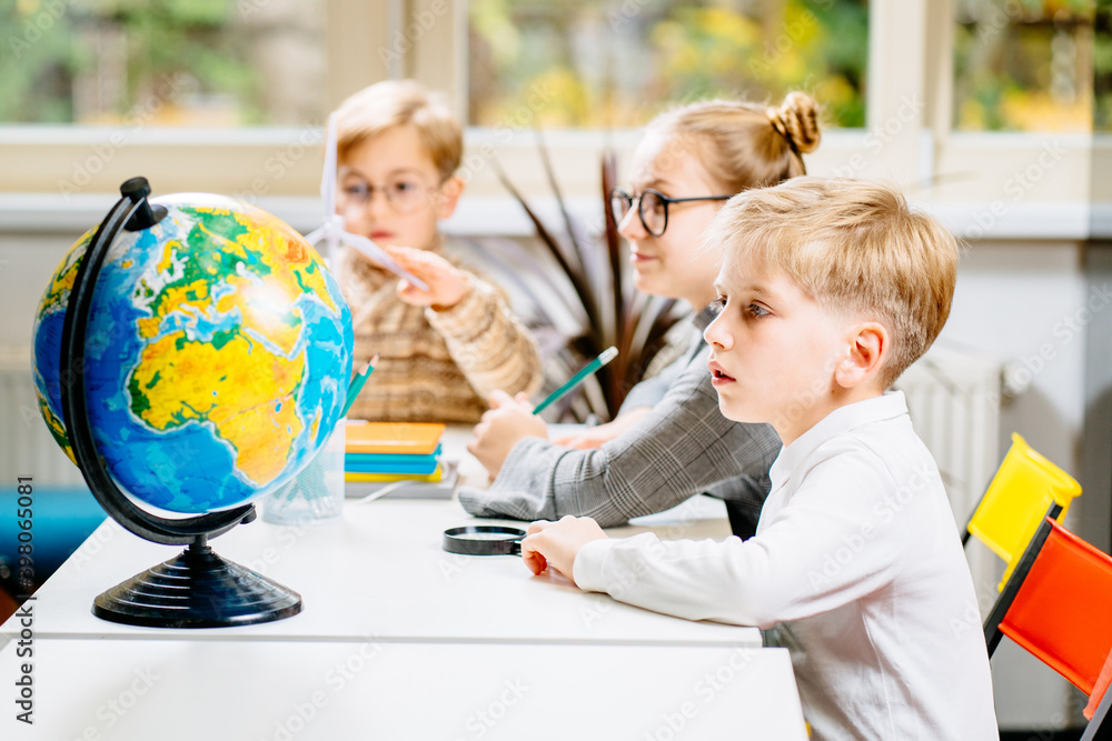 Side view of cute thoughtful school boy sits at a table in the ...
