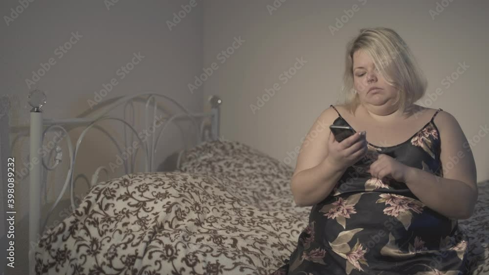 Exhausted fat woman sets an alarm clock on her smart phone and falls on ...