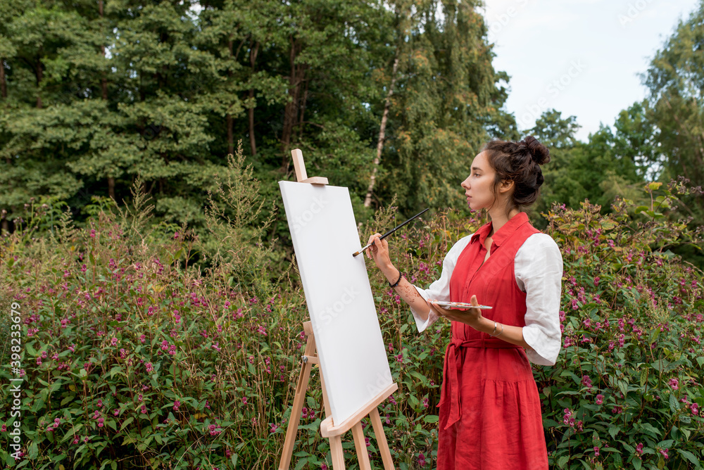 Getting started, woman in red dress, begins to paint picture, in summer ...