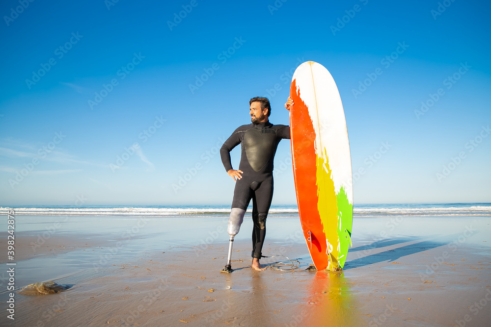 Confident handicapped man standing on sea beach with board. Attractive ...