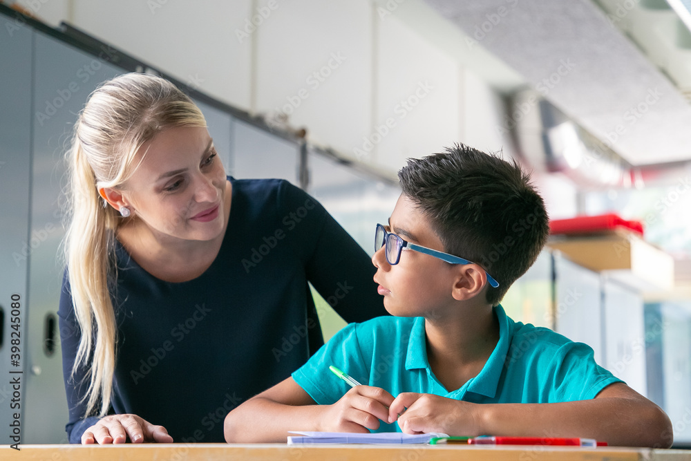 Cheerful school teacher giving help and support to schoolboy in class ...