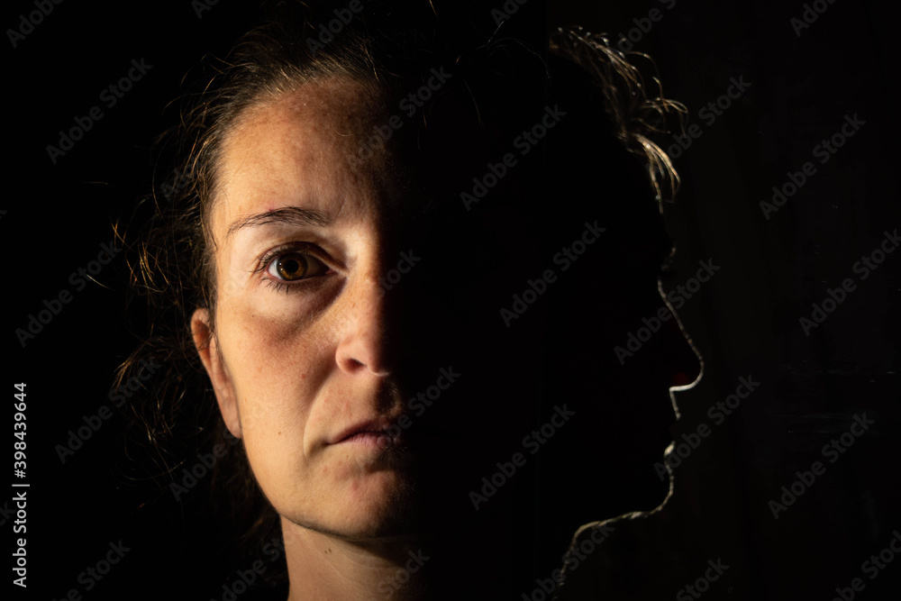 Dark portrait of a serious woman with only half an illuminated face on ...
