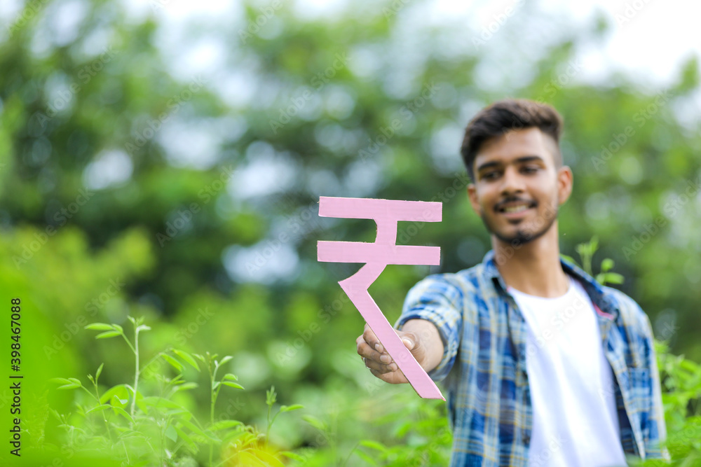 Young indian man holding indian rupees symbol in hand over nature ...