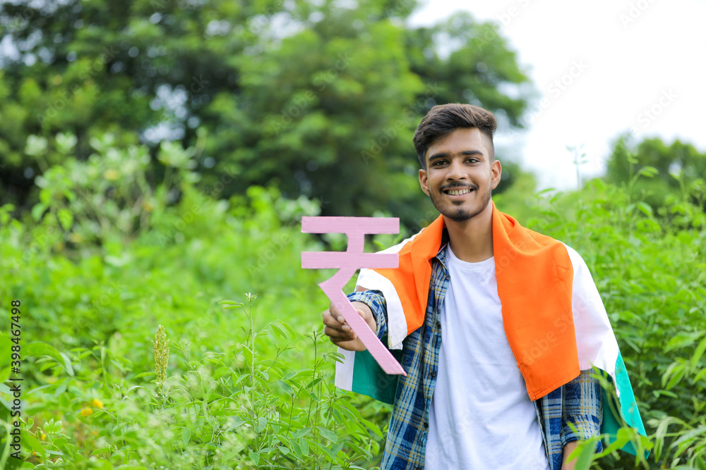 Young indian man holding indian rupees symbol in hand over nature ...