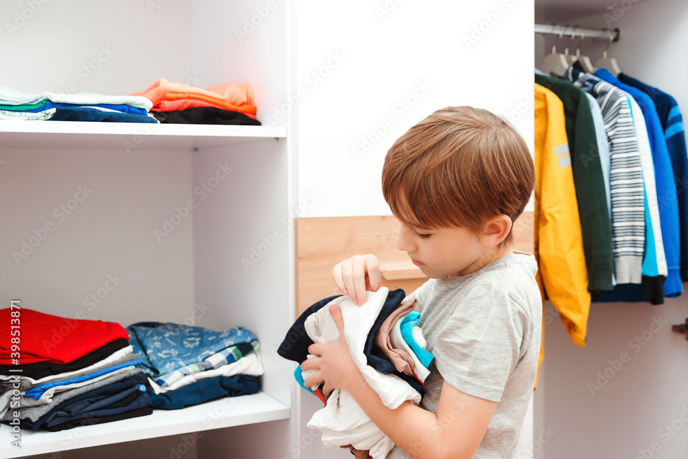 Boy organizing clothes in wardrobe, close up. Kid putting stack of ...