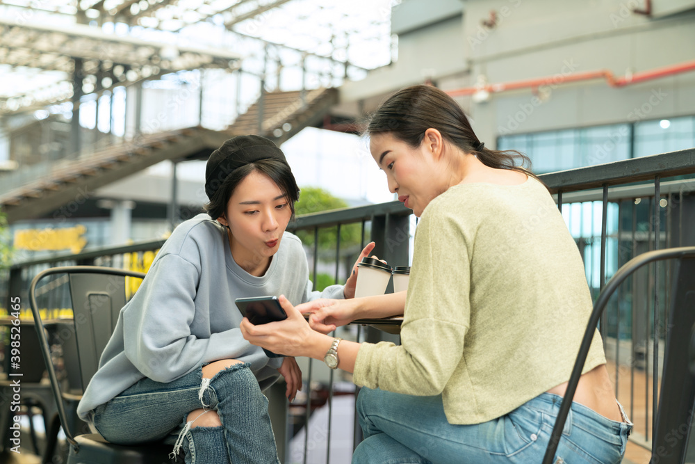 Two young woman having fun with smartphones at coffee breaks in public ...