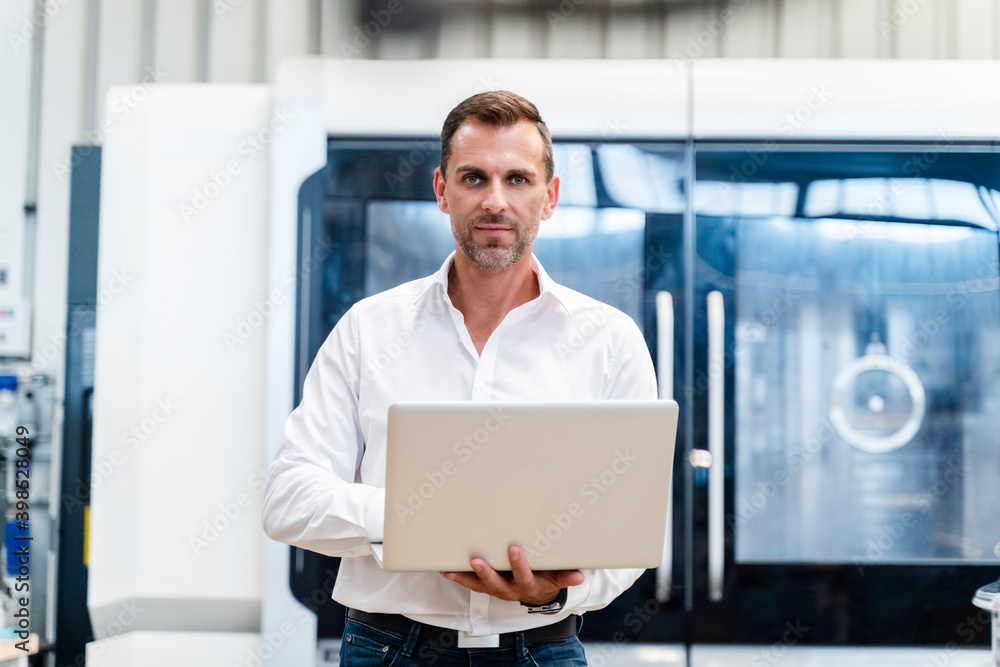 Confident businessman holding laptop while standing in industry Stock ...