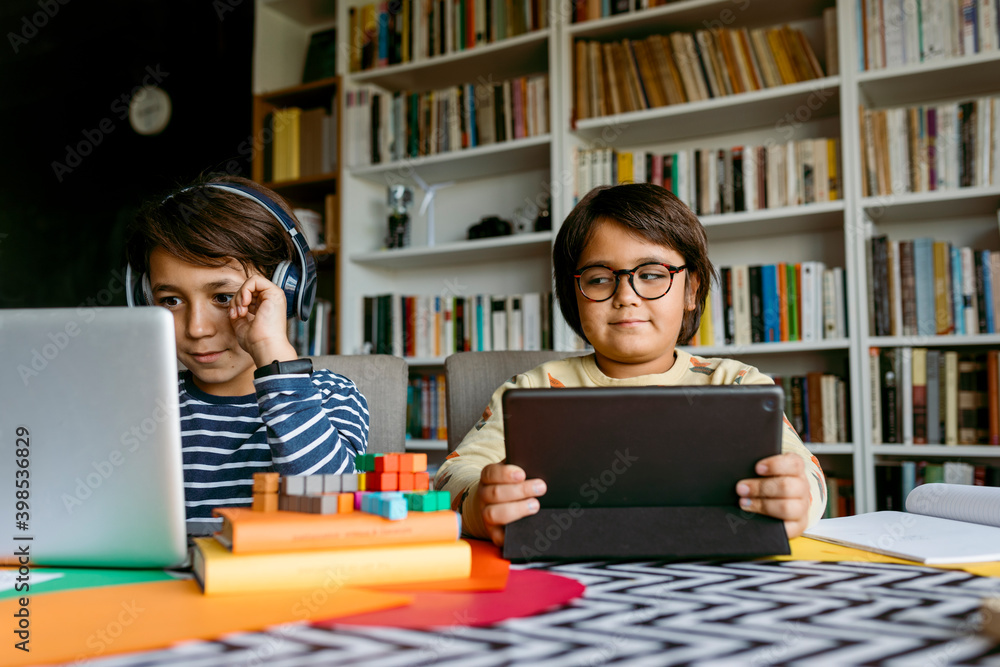 Smiling boy e-learning through laptop while male friend peeking at home ...