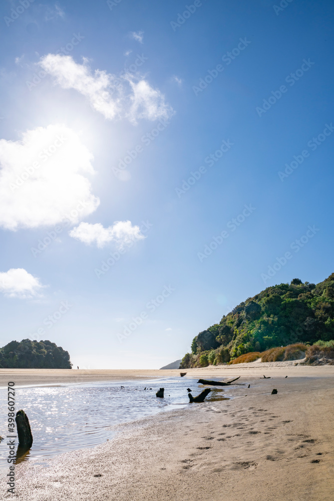 Shallow stream across low tide beach looking into sun in idyllic summer ...