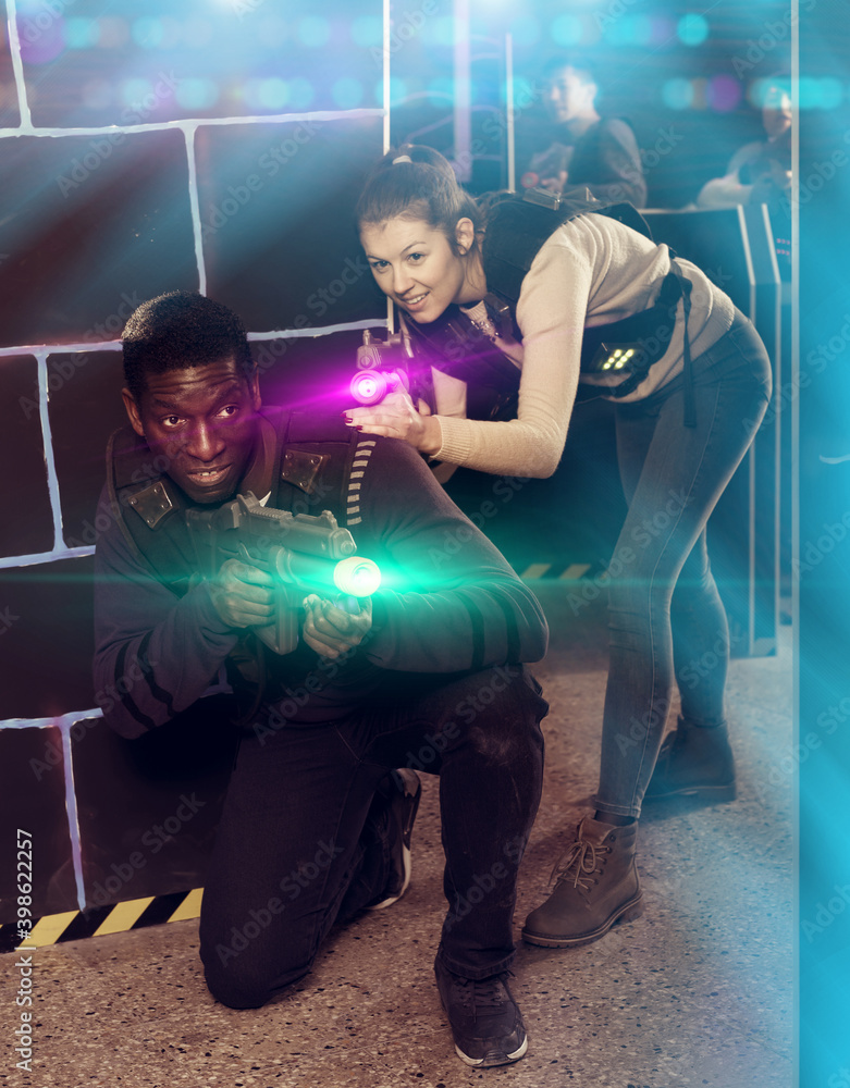 Young laser tag players of different nationalities aiming laser guns at ...