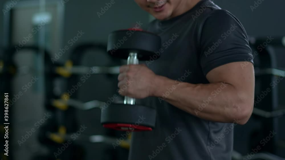 B-roll footage, muscular Asian young man lifting up a dumbbell in gym ...