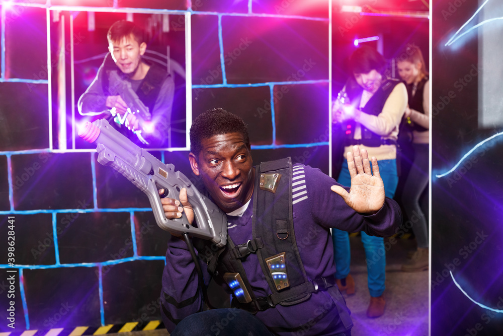 Cheerful African American man aiming laser pistol at other players ...