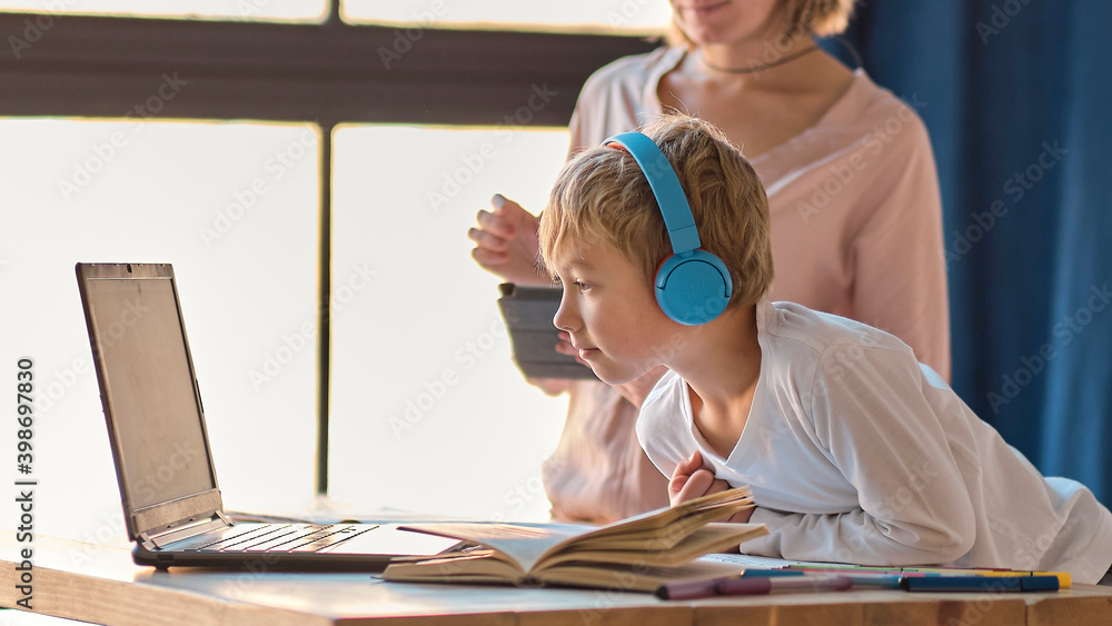 mom helping young son with laptop to do homework. Young woman teaching ...