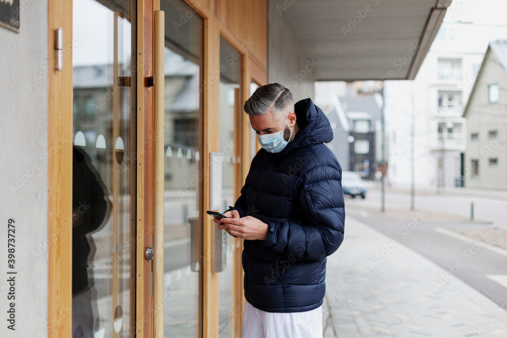 Man wearing face mask using phone in front of entrance door Stock Photo ...
