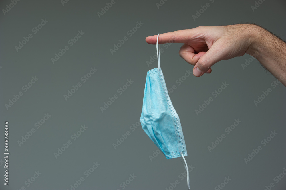 Caucasian male hand dangling a blue textile medical mask close up front ...
